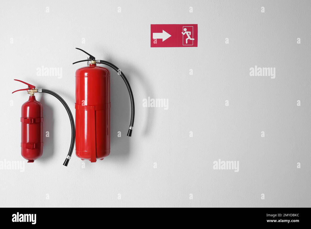 Different fire extinguishers and emergency exit sign on white wall ...