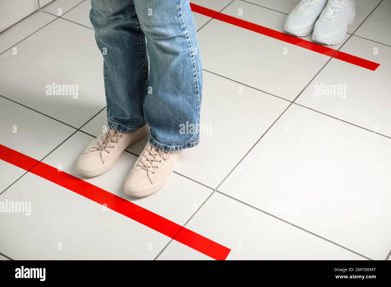 People standing in line behind taped floor markings for social distance ...