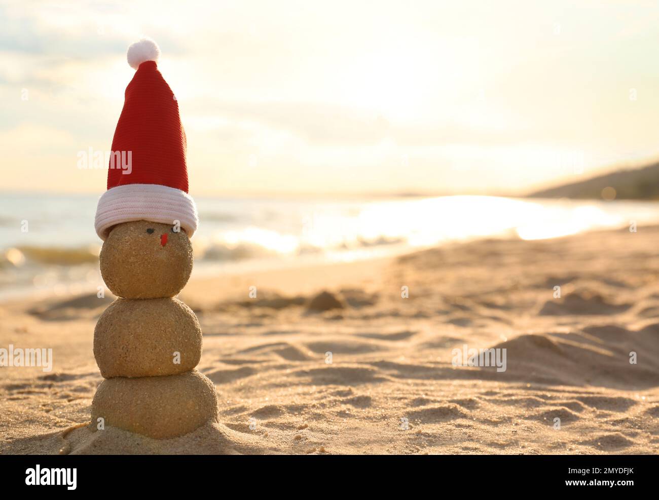 Snowman made of sand with Santa hat on beach near sea at sunset, space ...