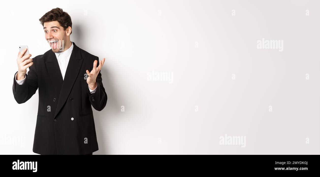 Portrait of happy smiling man in black suit, looking at smartphone ...