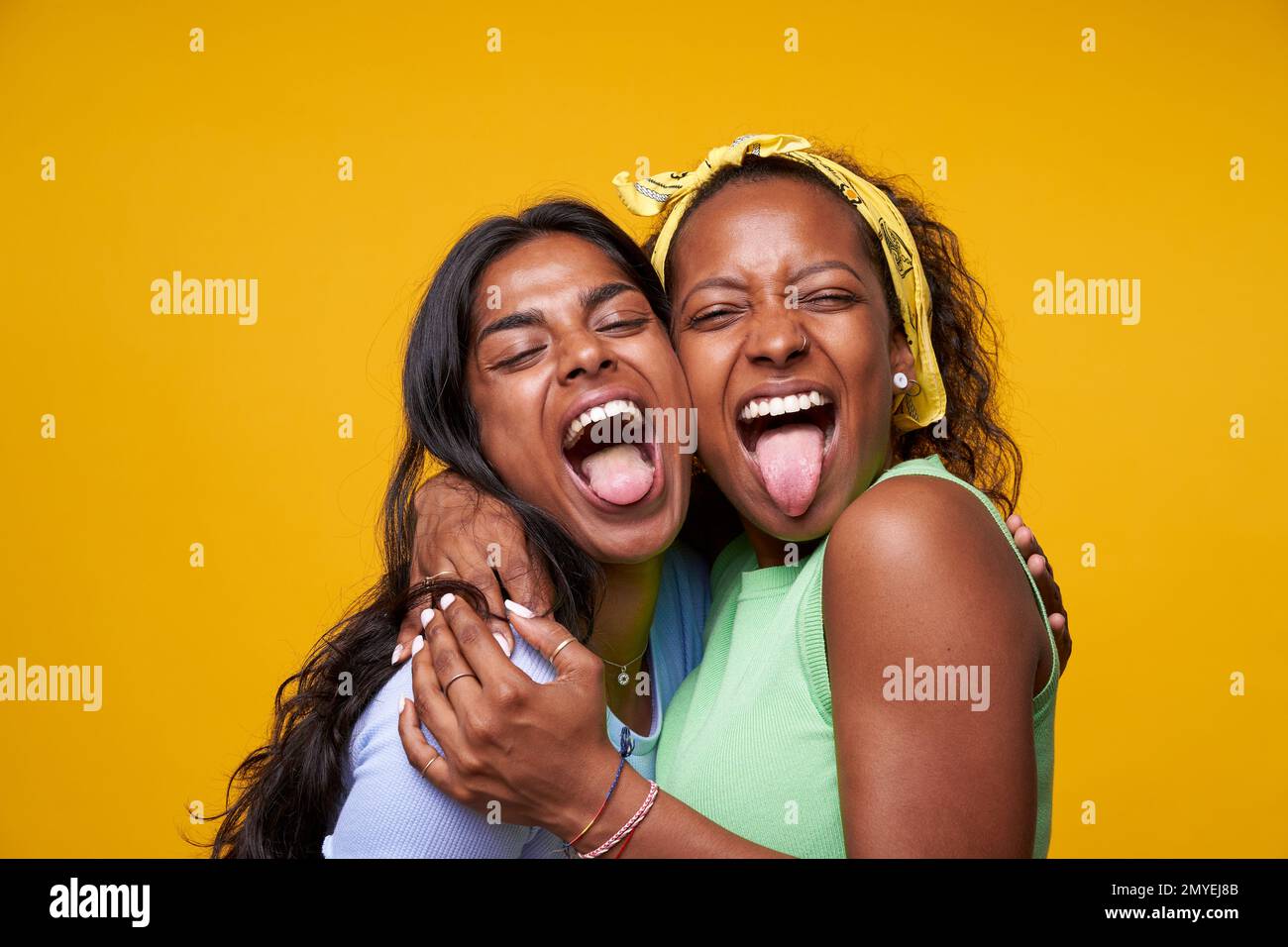 Two diversity pretty positive girls stick out your tongue hugging ...