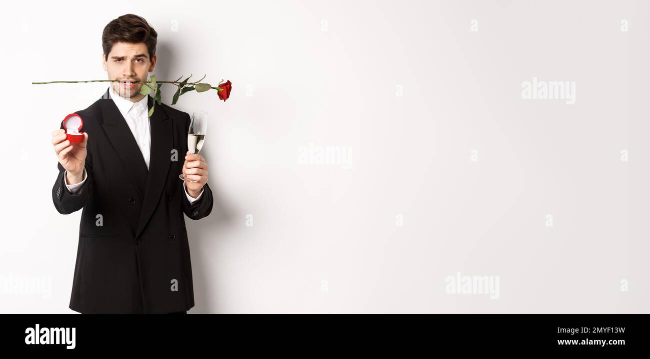Passionate young man in suit making a proposal, holding rose in teeth ...