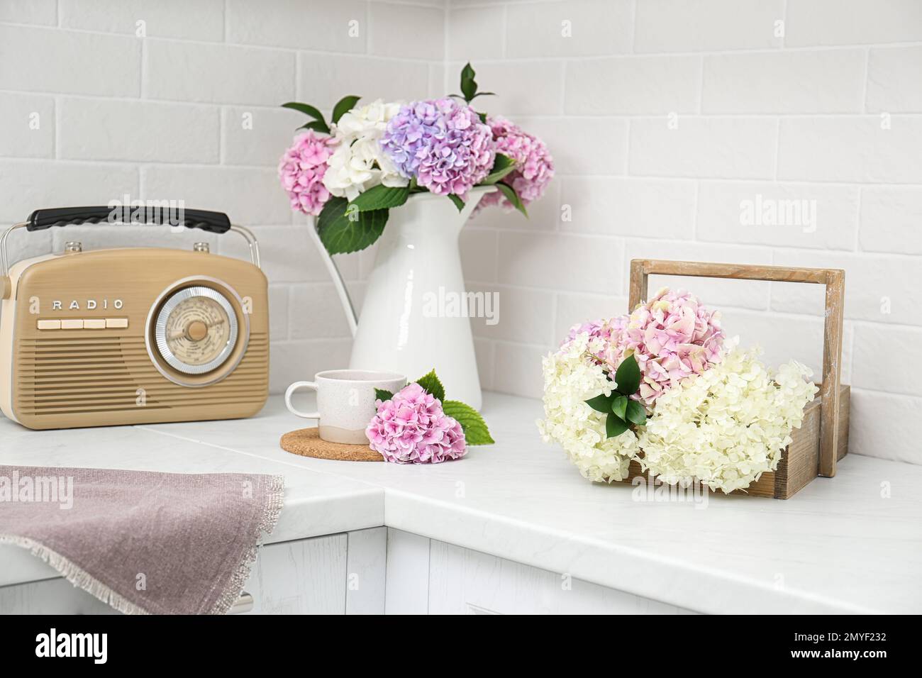 Beautiful hydrangea flowers, cup and radio set on light countertop ...