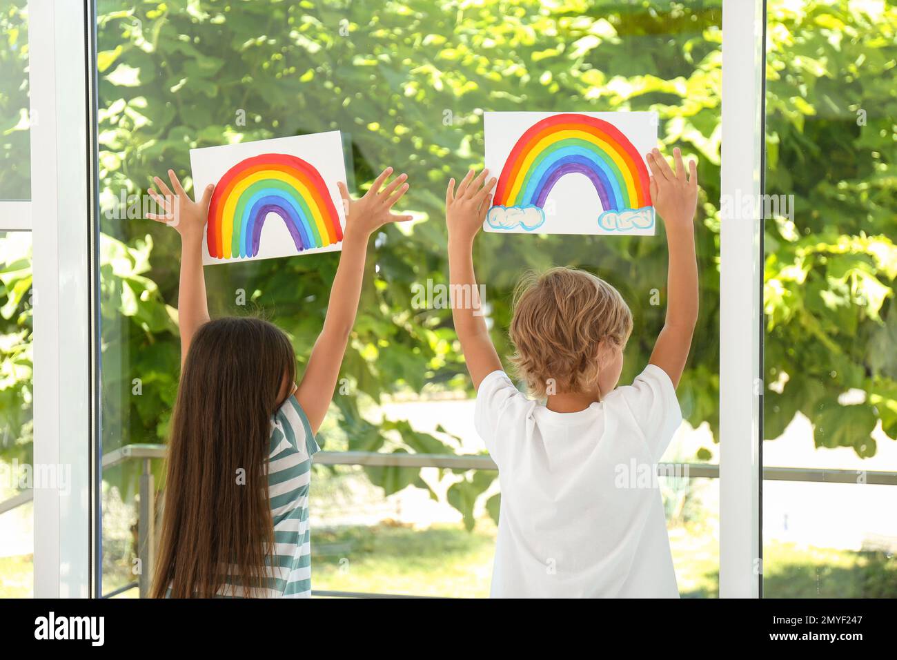Little children holding rainbow paintings near window indoors, back ...