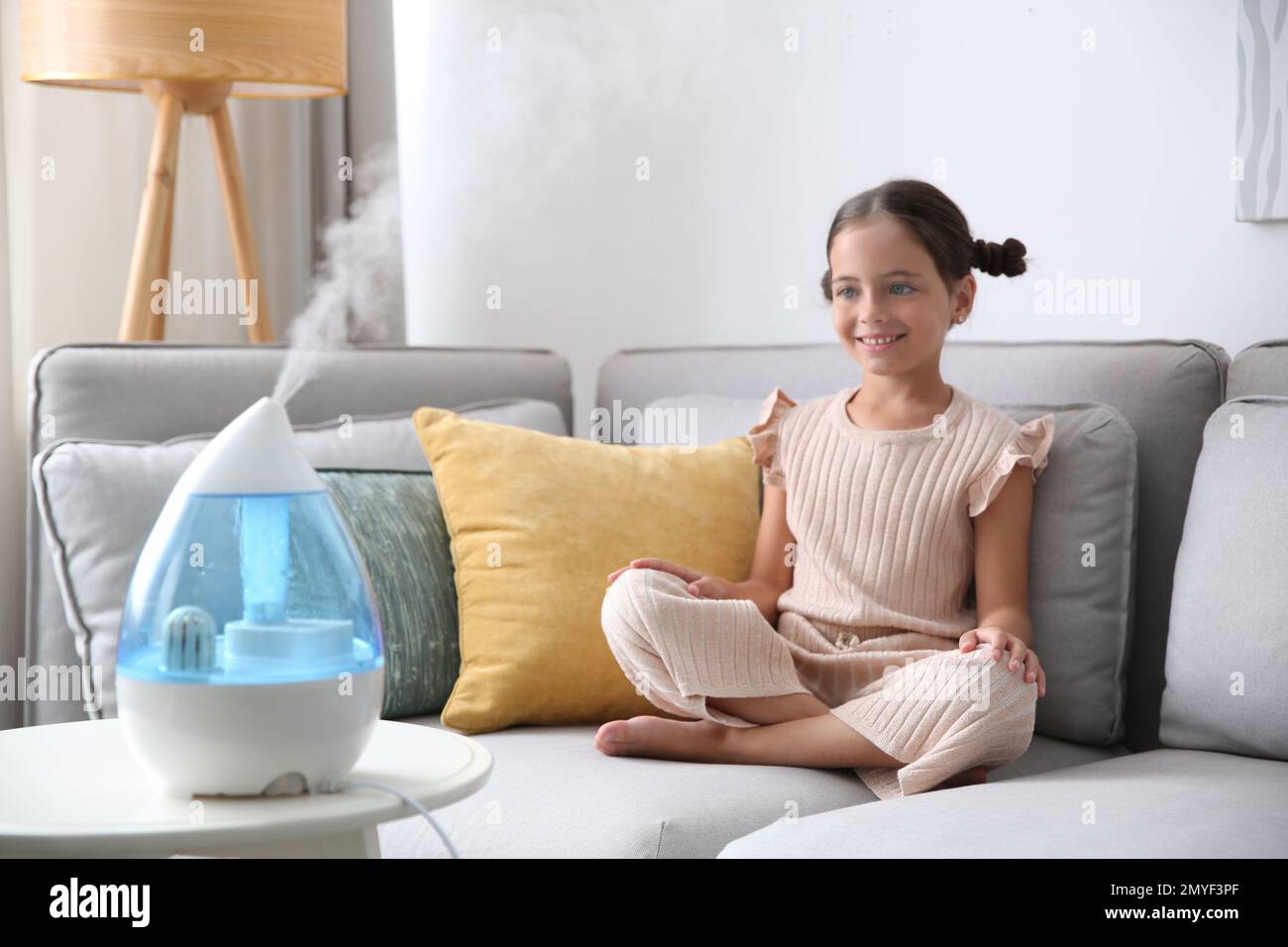 Little girl on sofa in room with modern air humidifier Stock Photo - Alamy