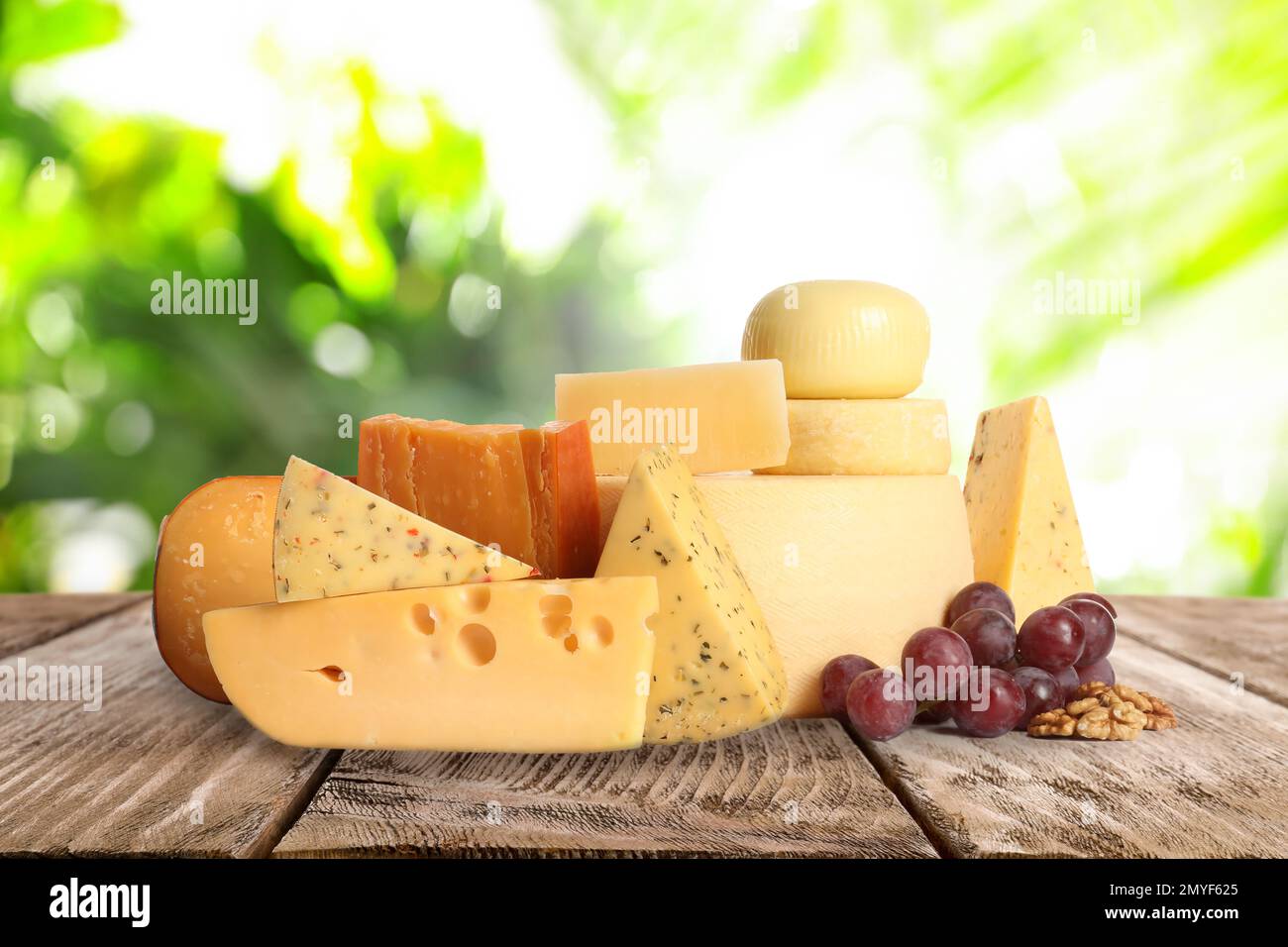 Different types of delicious cheeses on wooden table outdoors. Dairy ...