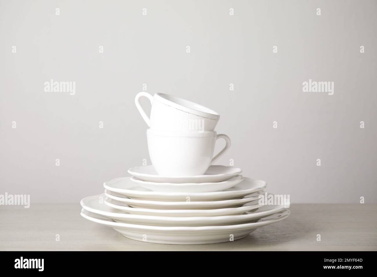 Stack of clean plates and cups on table against white background Stock ...