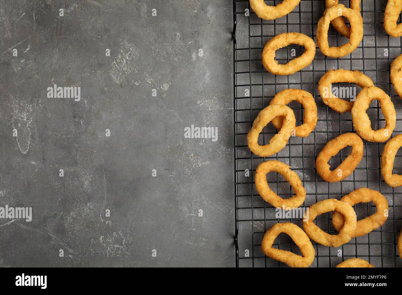 Cooling rack with fried onion rings on grey table, top view. Space for ...