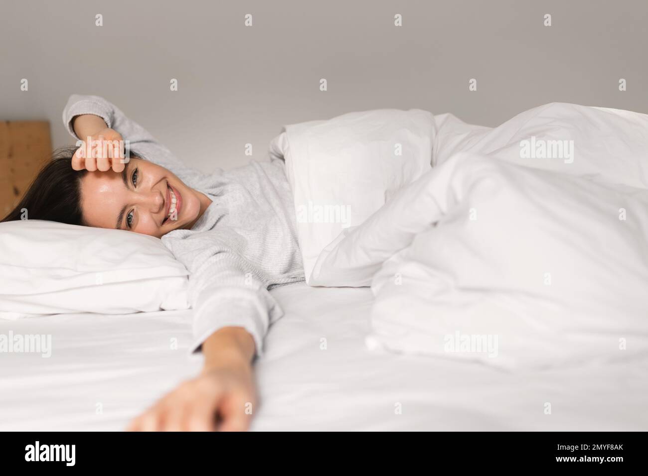 Smiling young european female sleeping on white bed, waking up ...