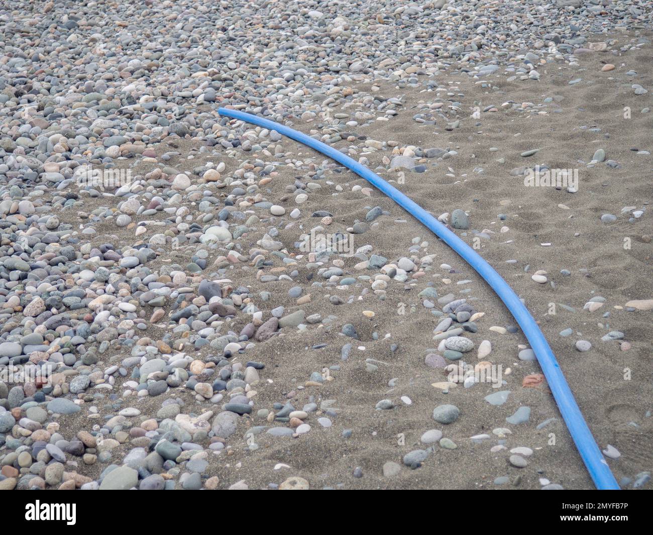 Cable on black sand. The cable sticks out of the ground. Electrical ...