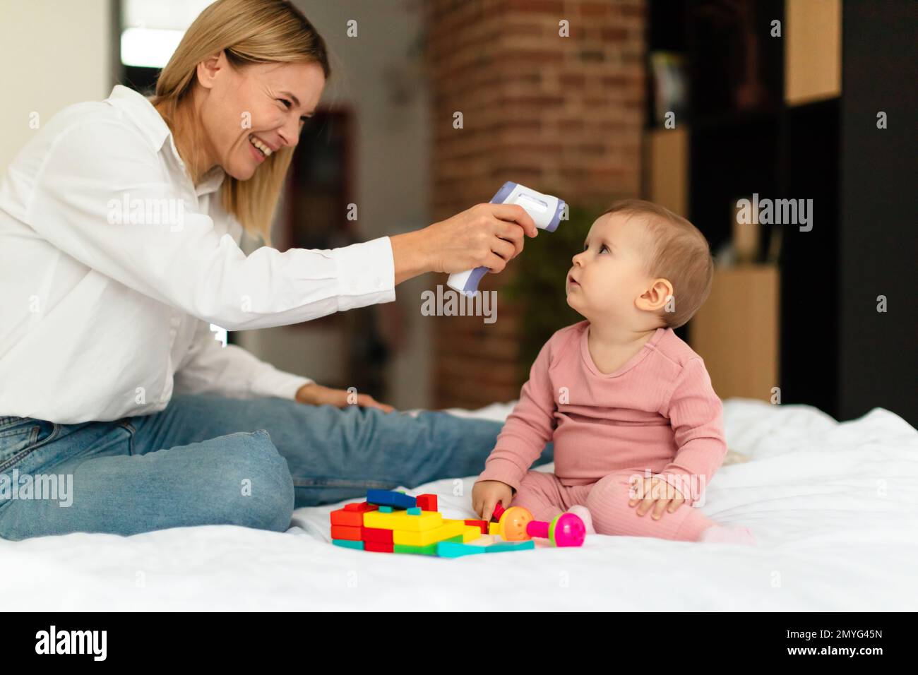 Mother measuring temperature with contactless digital thermometer of her little daughter child ...
