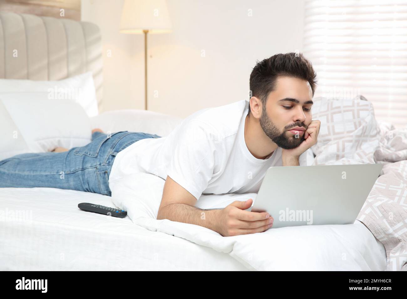 Lazy young man with laptop on bed at home Stock Photo - Alamy