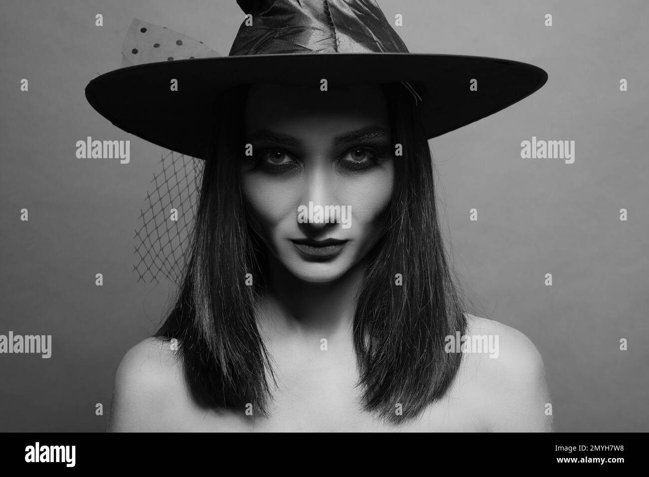 Mysterious witch wearing hat on dark background. Black and white effect ...