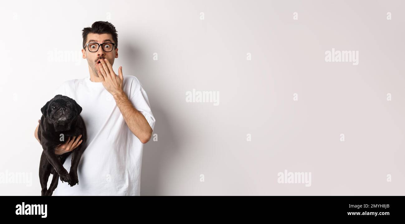 Image of handsome young man holding cute dog and gasping surprised. Pet ...