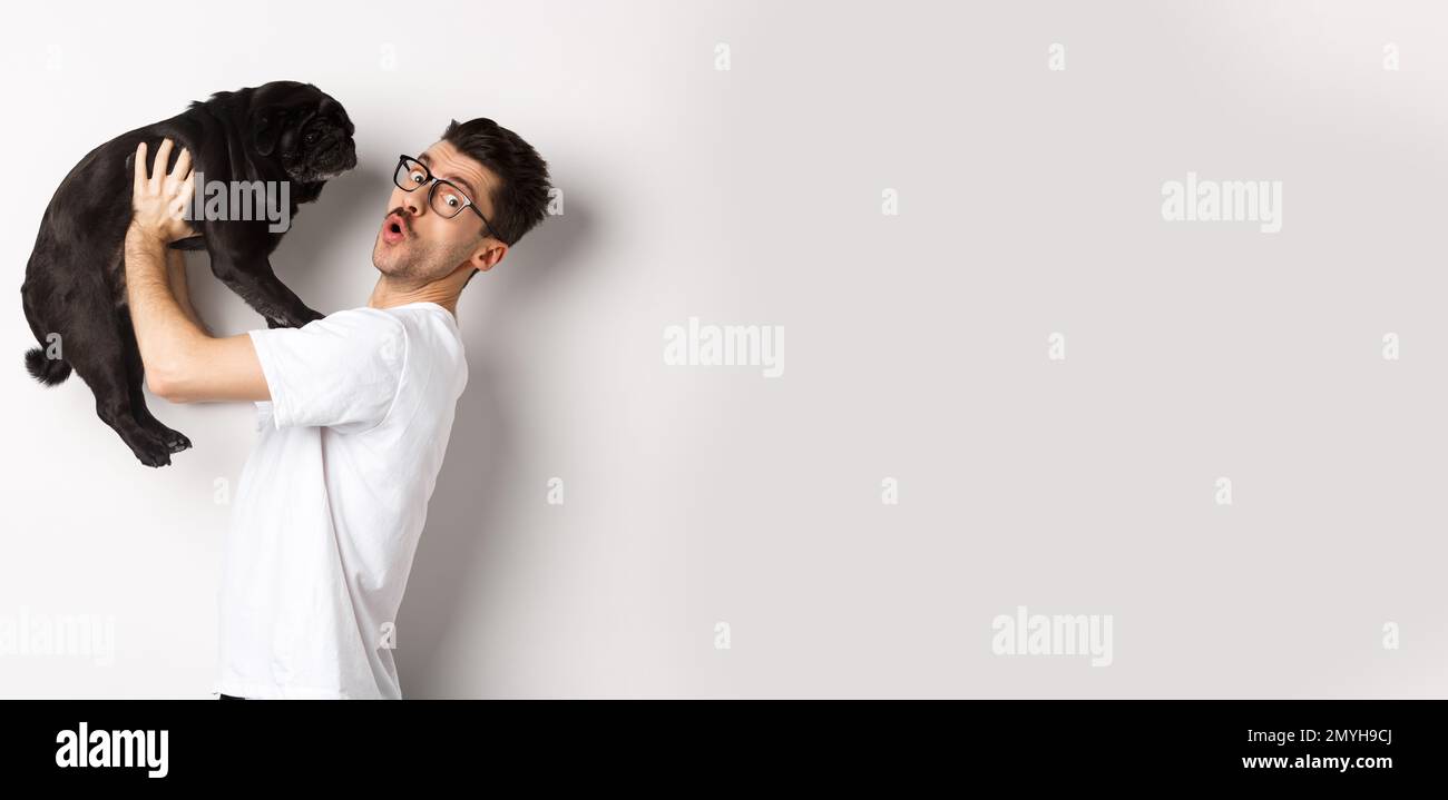 Image of handsome young man loving his pug. Dog owner holding puppy and ...