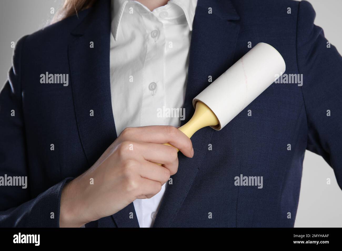 Woman cleaning dark blue jacket with lint roller on grey background ...