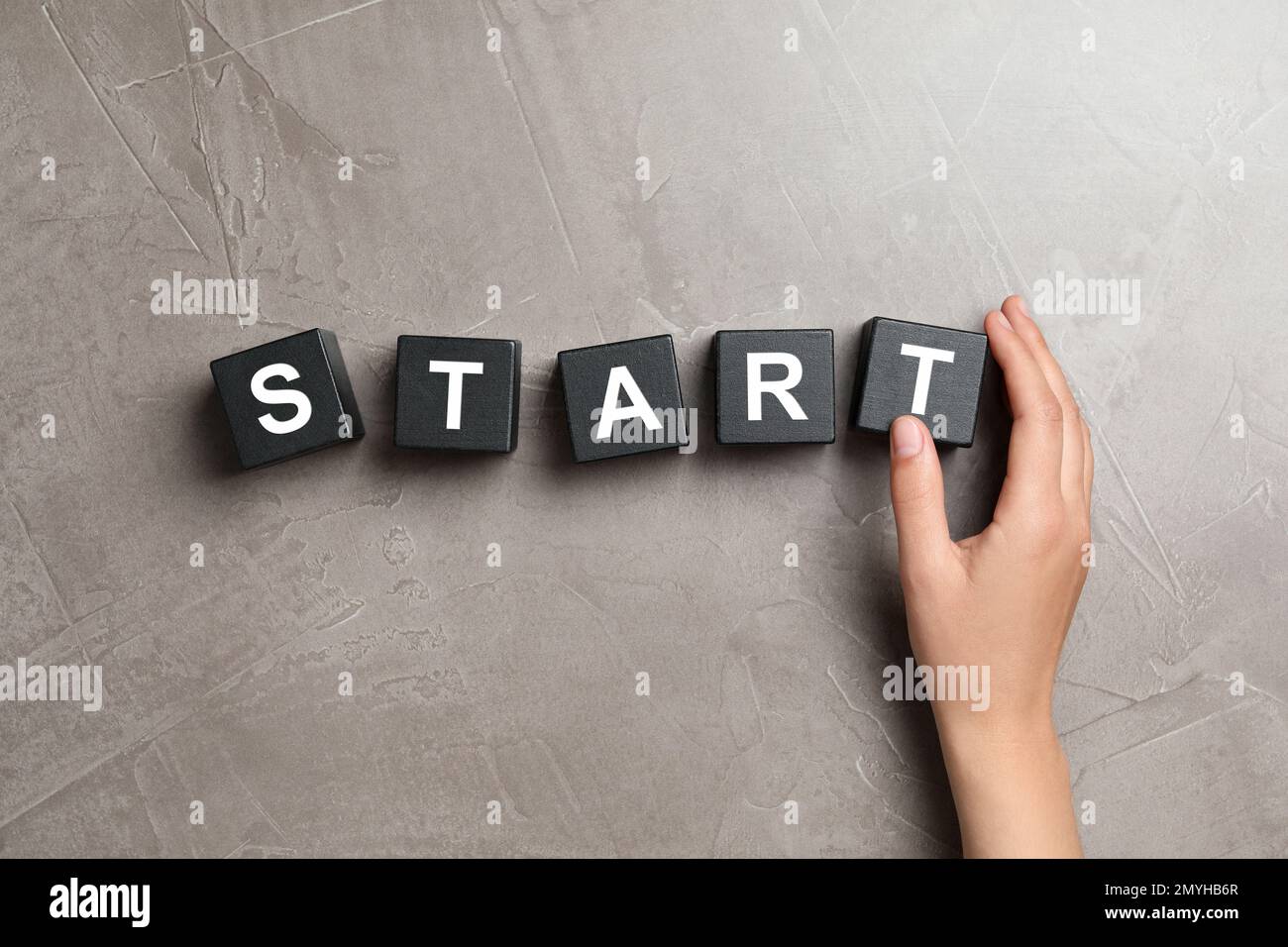 Woman making word START with black cubes on beige stone background, top ...
