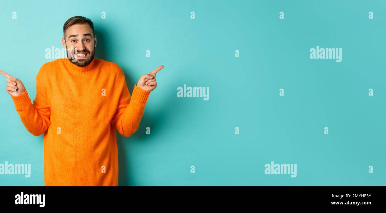 Confused handsome man shrugging indecisive, pointing fingers sideways ...