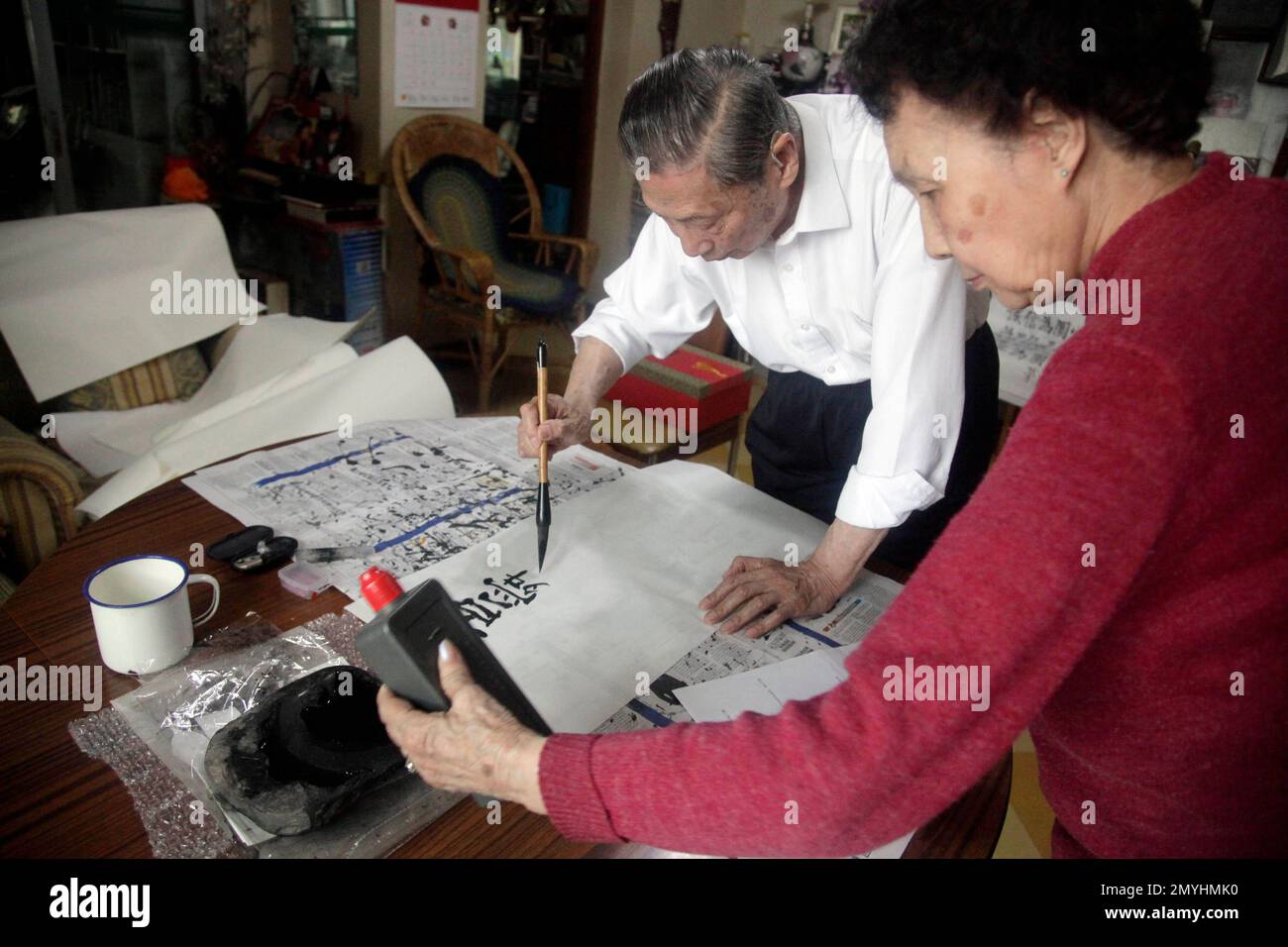 In this May 25, 2016 photo, Mao Yushi writes calligraphy as his wife ...