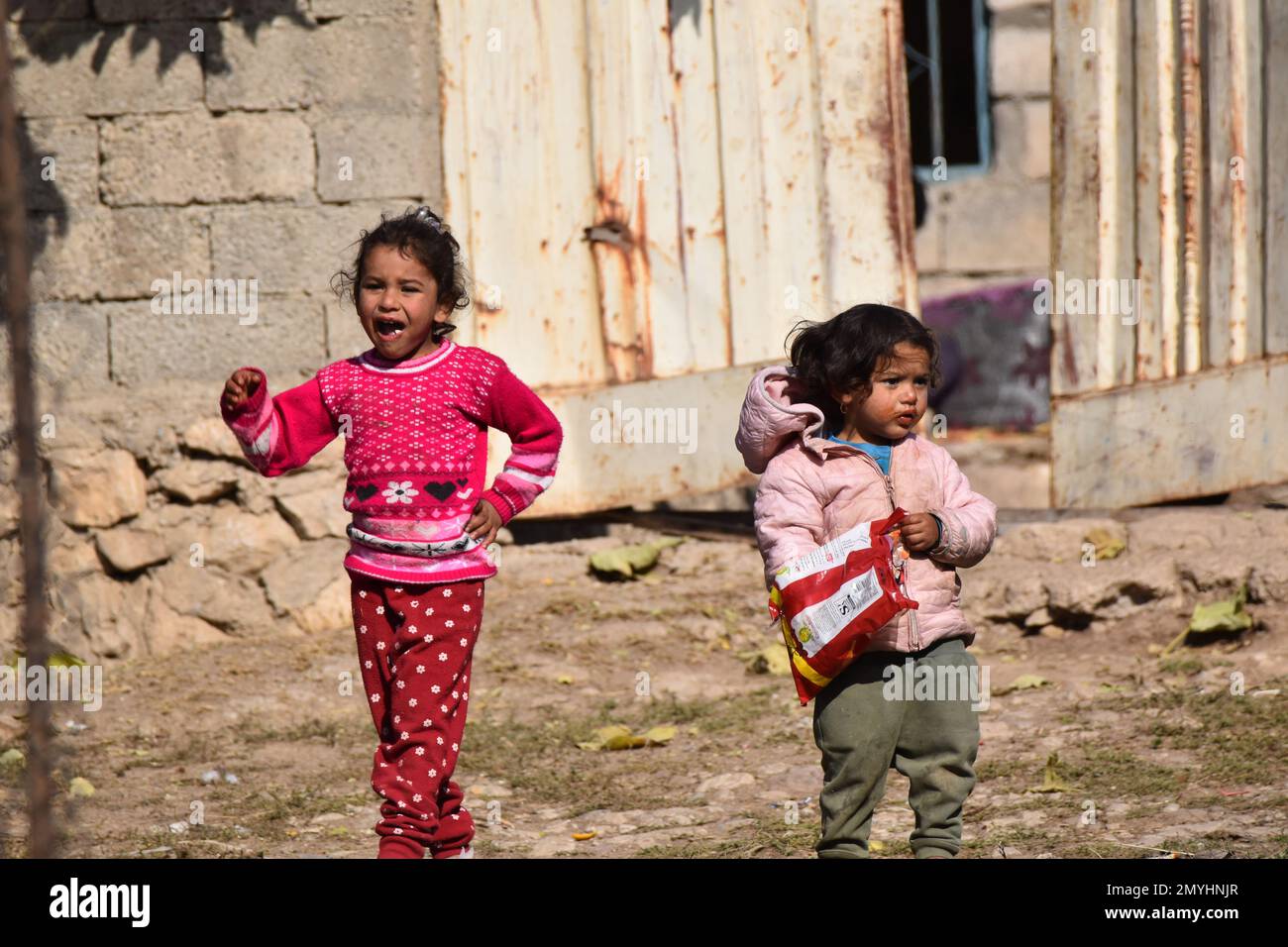 Two little girls, one with her hand in a bag of chips, watch as ...