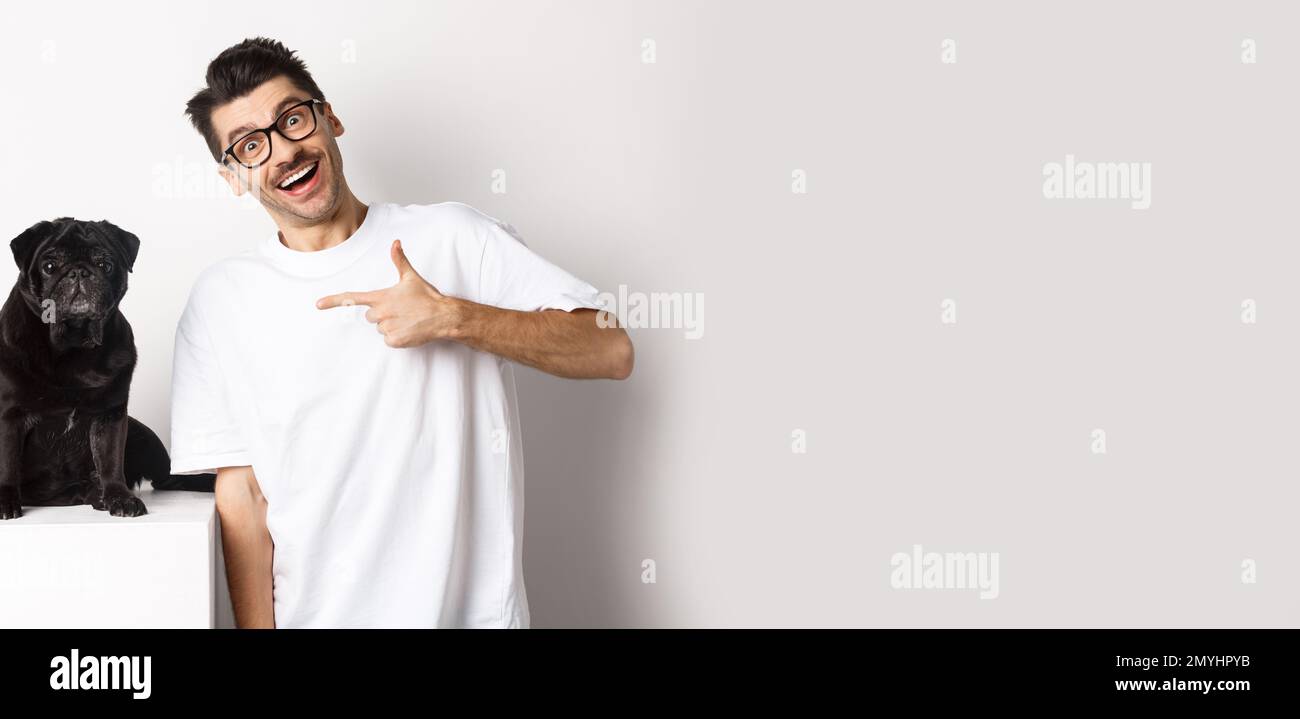 Happy young man showing his cute dog, pointing finger at black pug and ...