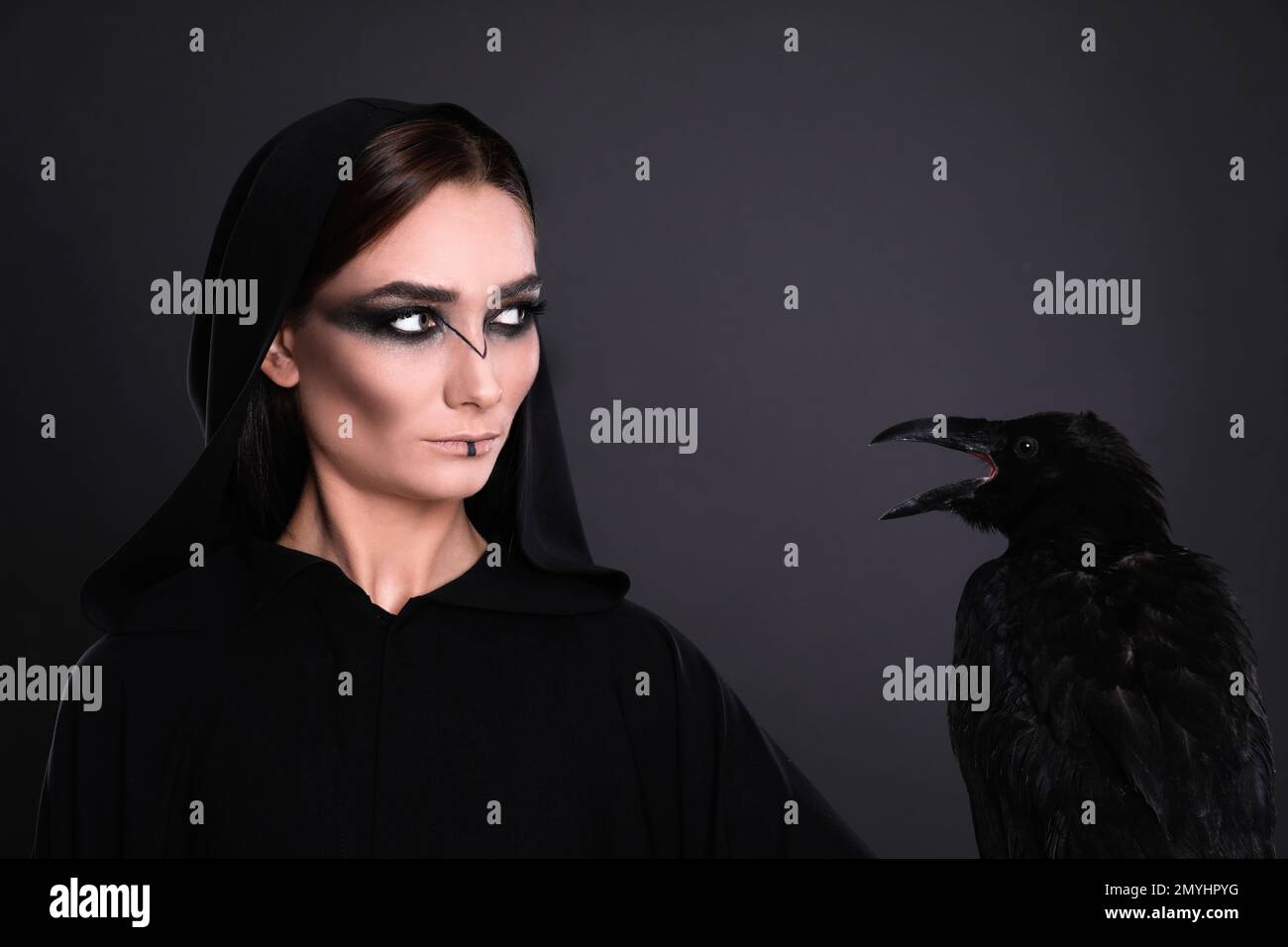 Mysterious witch with raven on black background Stock Photo - Alamy