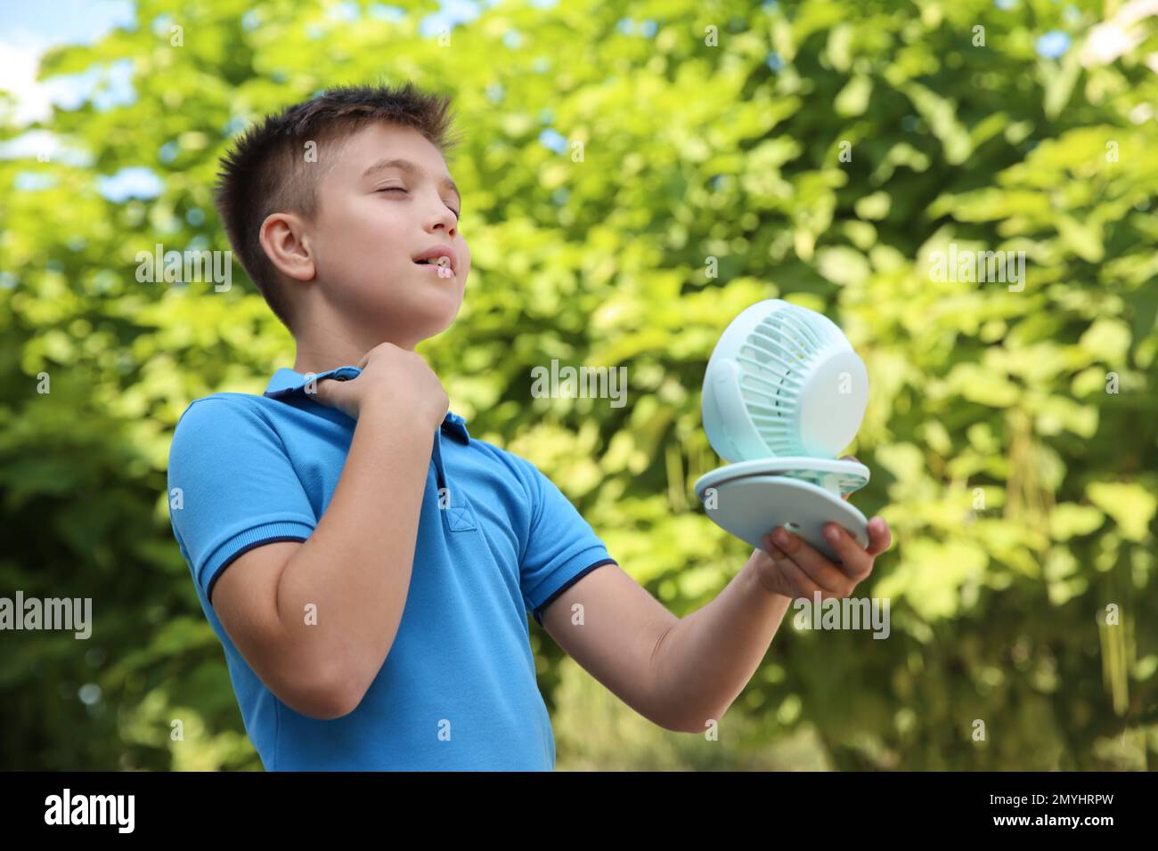 Little boy enjoying air flow from portable fan outdoors. Summer heat ...