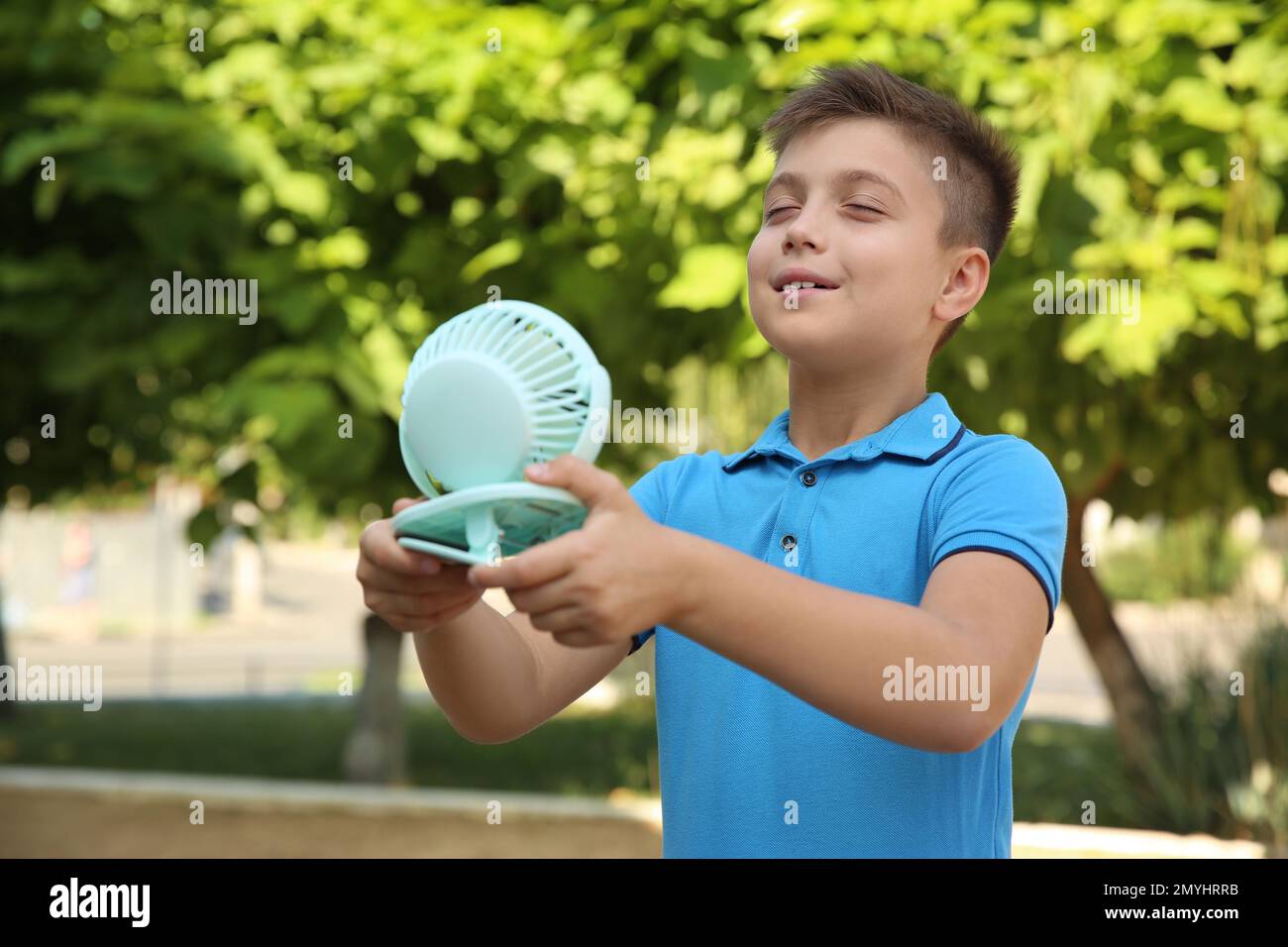 Little boy enjoying air flow from portable fan outdoors. Summer heat ...