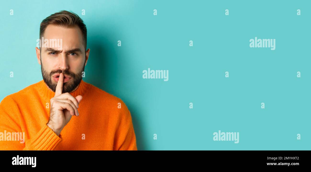 Close-up of annoyed frowning man shushing at camera, press finger to ...