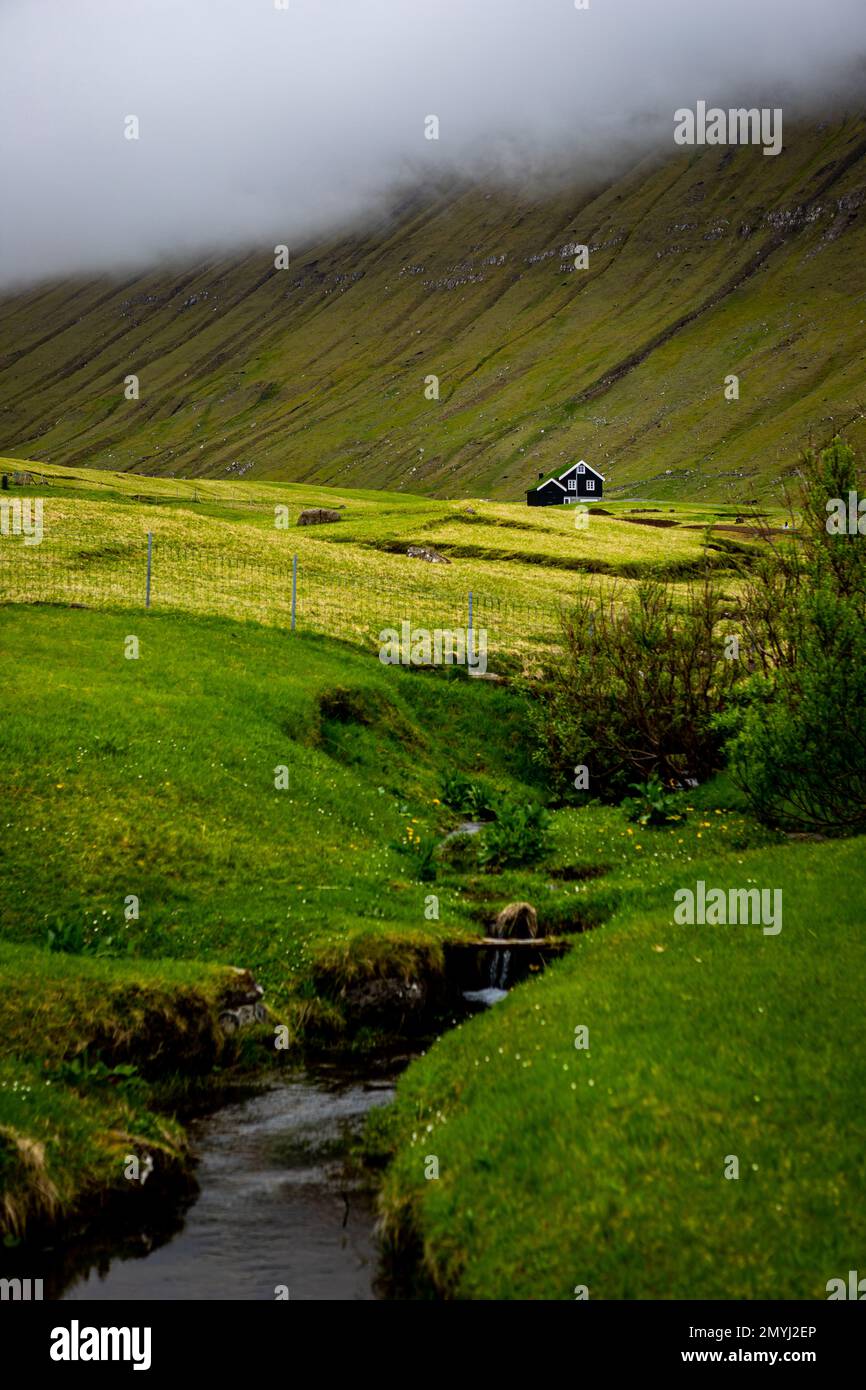 A narrow stream leading to a black house with grass roof outside of ...
