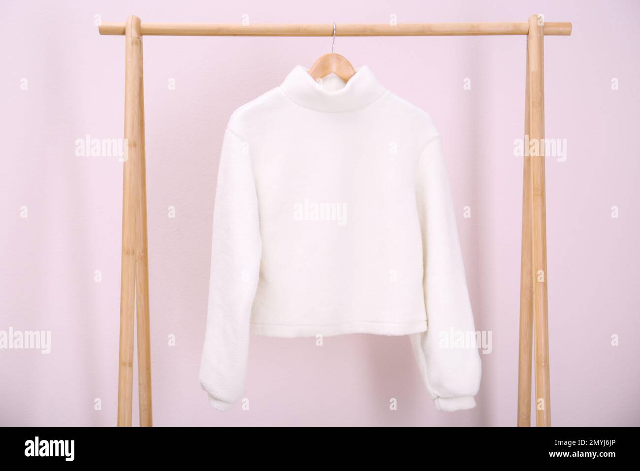 Stylish knitted sweater hanging on clothing rack near pink wall Stock ...