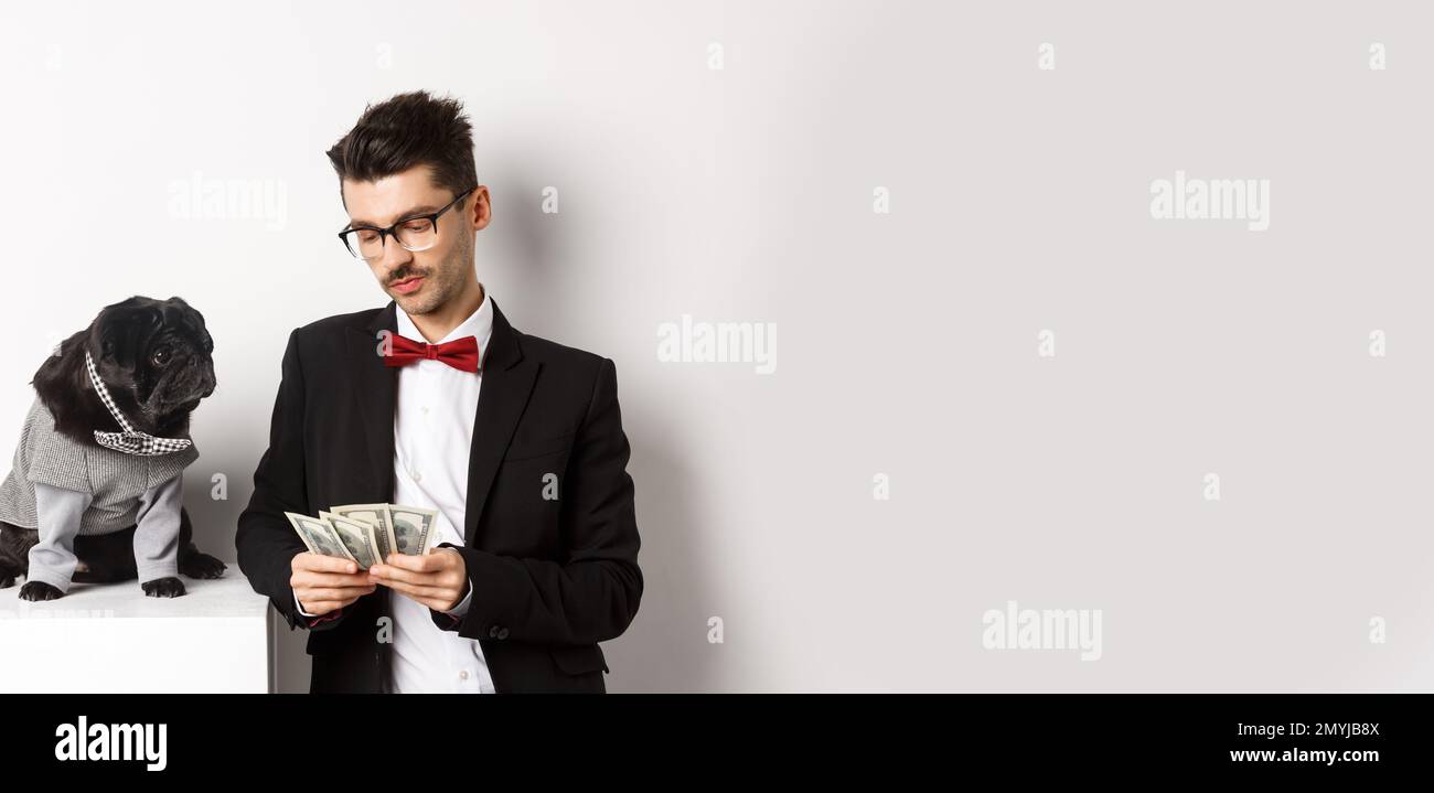 Handsome young man in suit standing near black pug in costume and ...