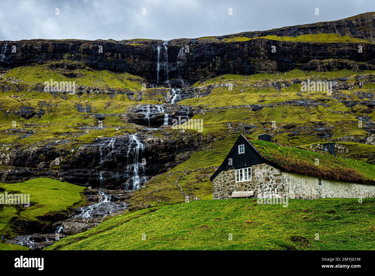 Rocky waterfall and traditional stone house with grass roof in town of ...