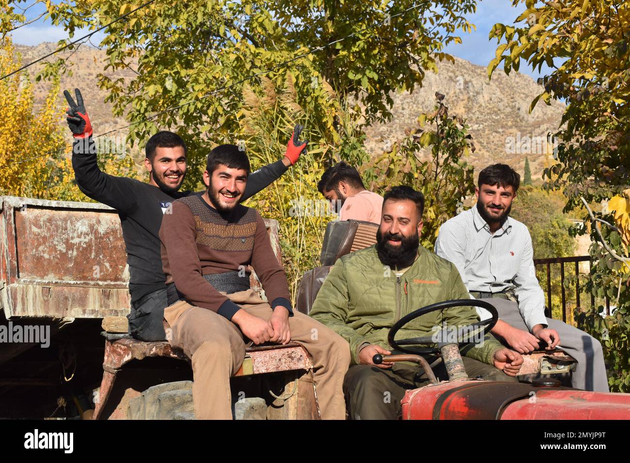 Five smiling men ride an old, red tractor in a Kurdish Iraqi village ...