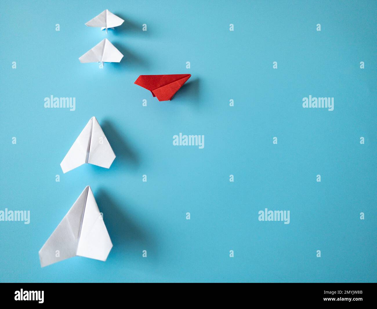 Red paper plane origami leaving other white planes on blue background ...