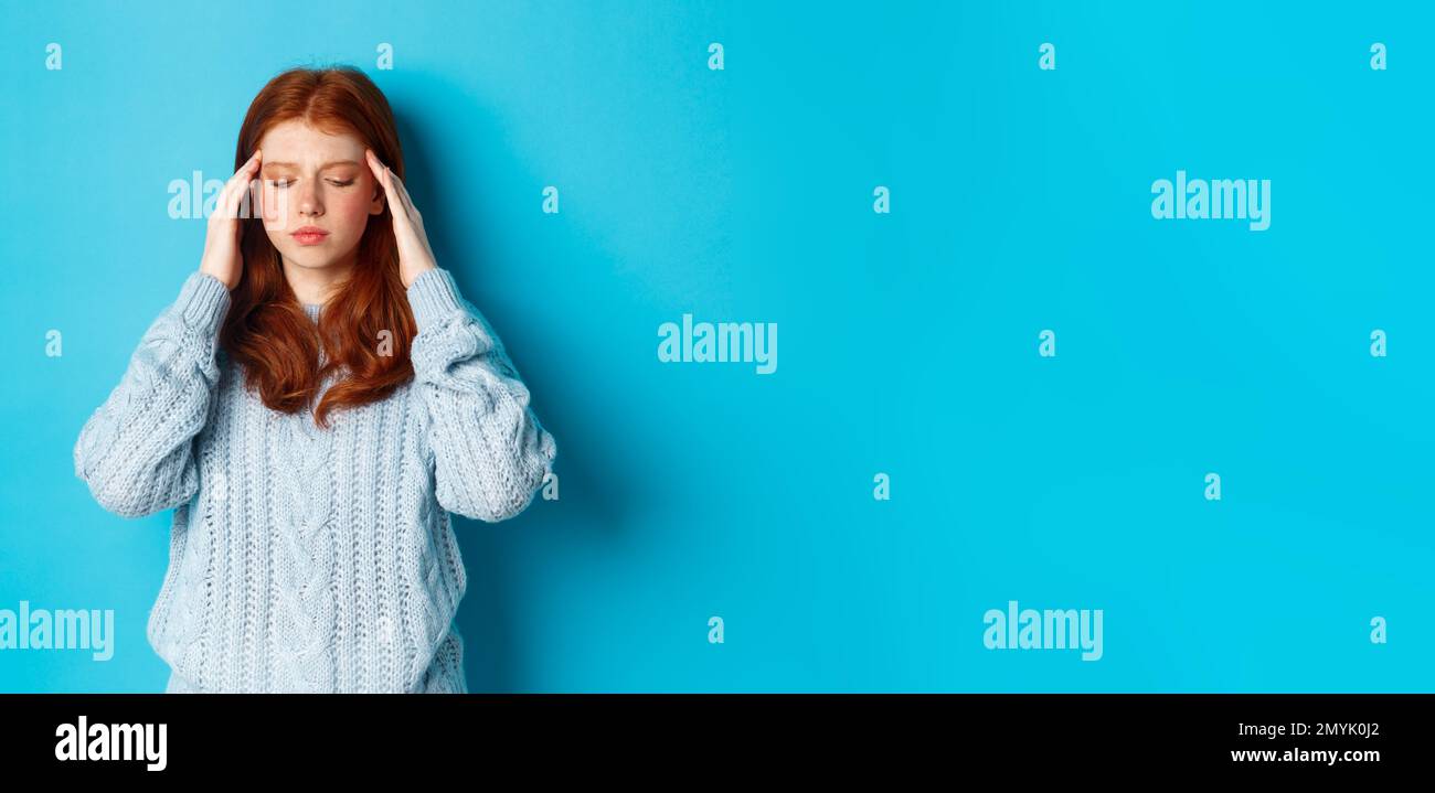 Distressed teenage redhead girl touching head, looking down with ...