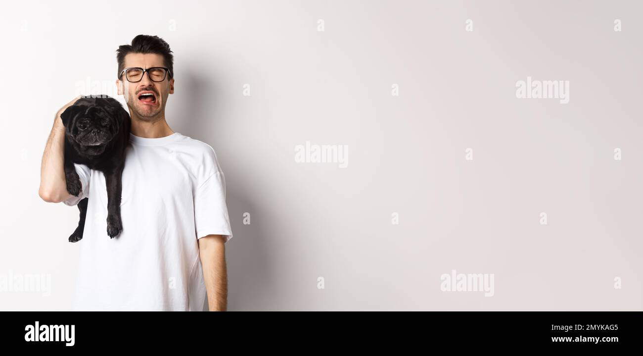 Sad dog owner crying, holding cute black pug on shoulder and looking ...