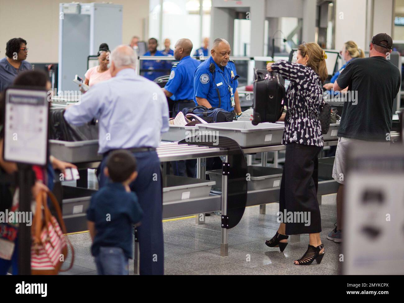 A TSA official helps passengers load their carry-on belongings onto an ...