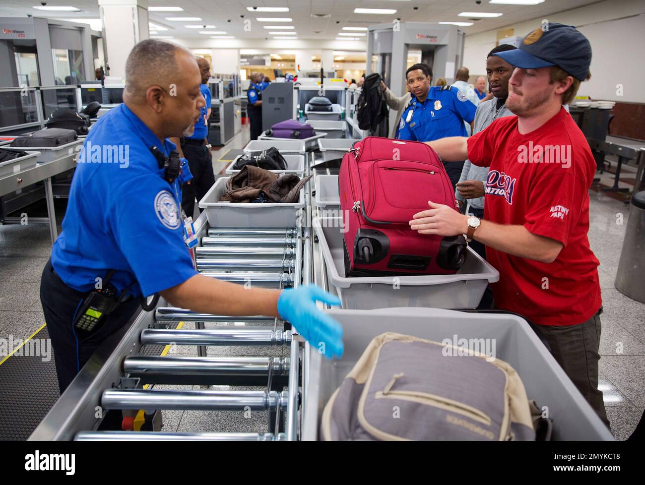 A TSA official helps passengers load their carry-on belongings onto an ...
