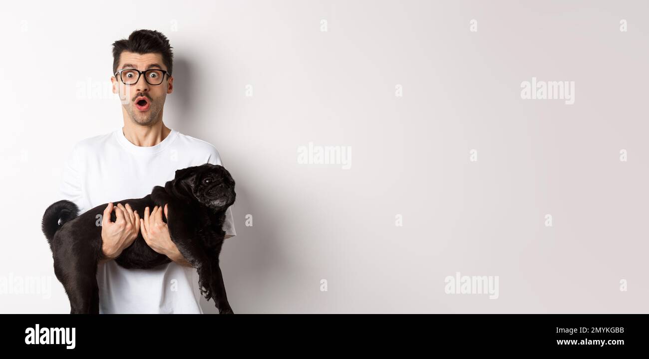 Surprised young man in glasses holding cute black pug, dog owner ...