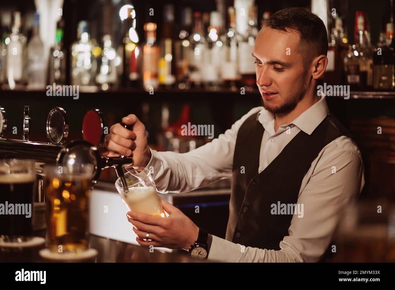 bartender pours draft beer into a glass from tap behind the bar counter ...