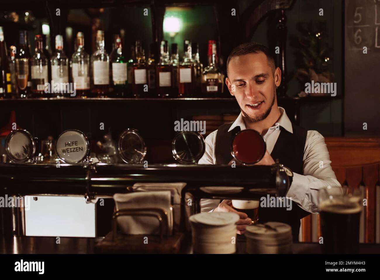 bartender pours draft beer into a glass from tap behind the bar counter ...