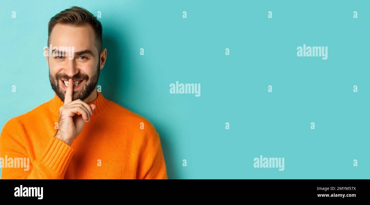 Close-up of handsome smiling man hushing, telling secret, standing over ...