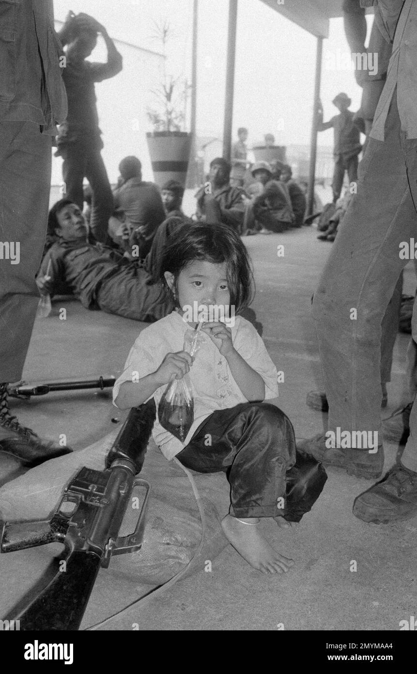 Leaning on a rifle, the daughter of a South Vietnamese soldier drinks ...