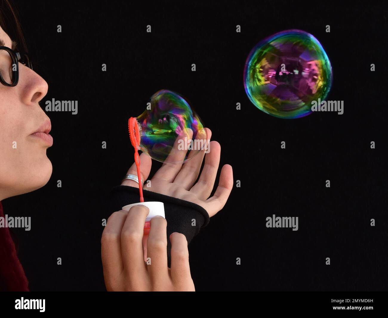 Woman blowing soap bubbles through immersion screen against black ...
