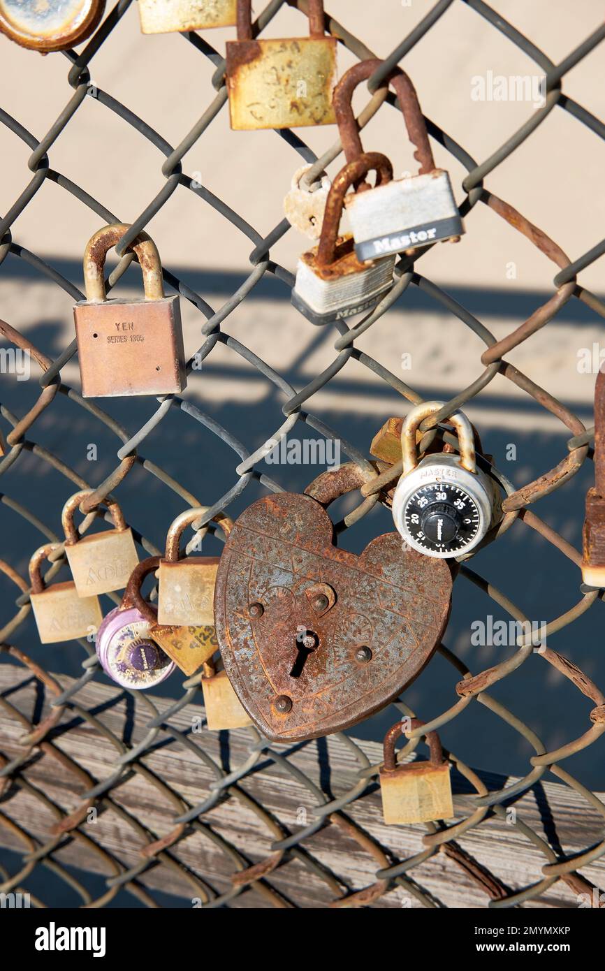 A rusty, heart shaped love lock padlock hangs on a chain link fence ...