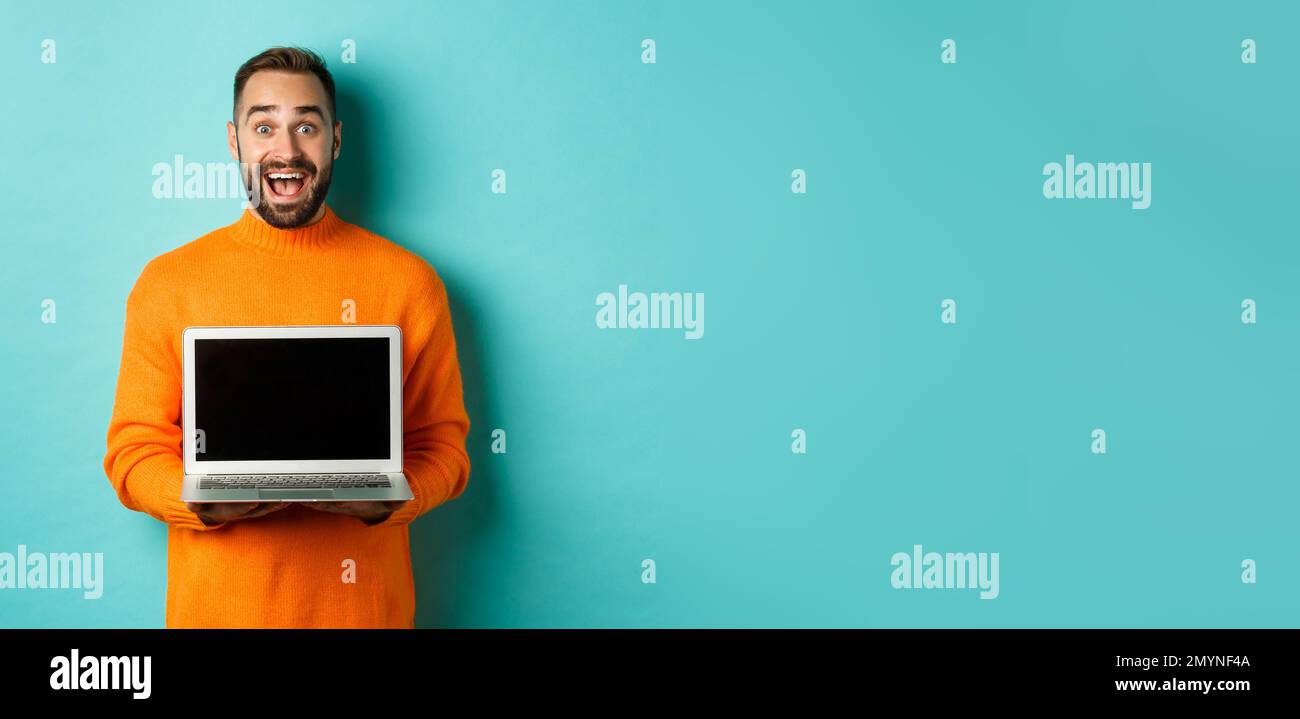 Handsome bearded man in orange sweater showing laptop screen ...
