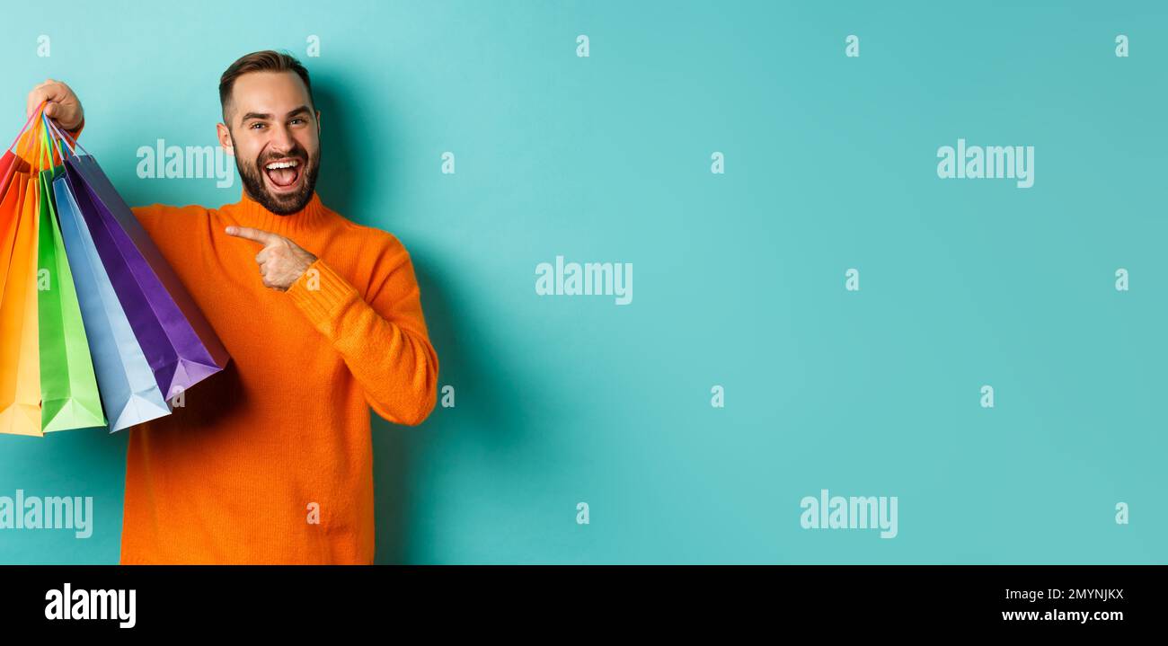 Happy handsome man holding shopping bags and smiling, pointing at ...