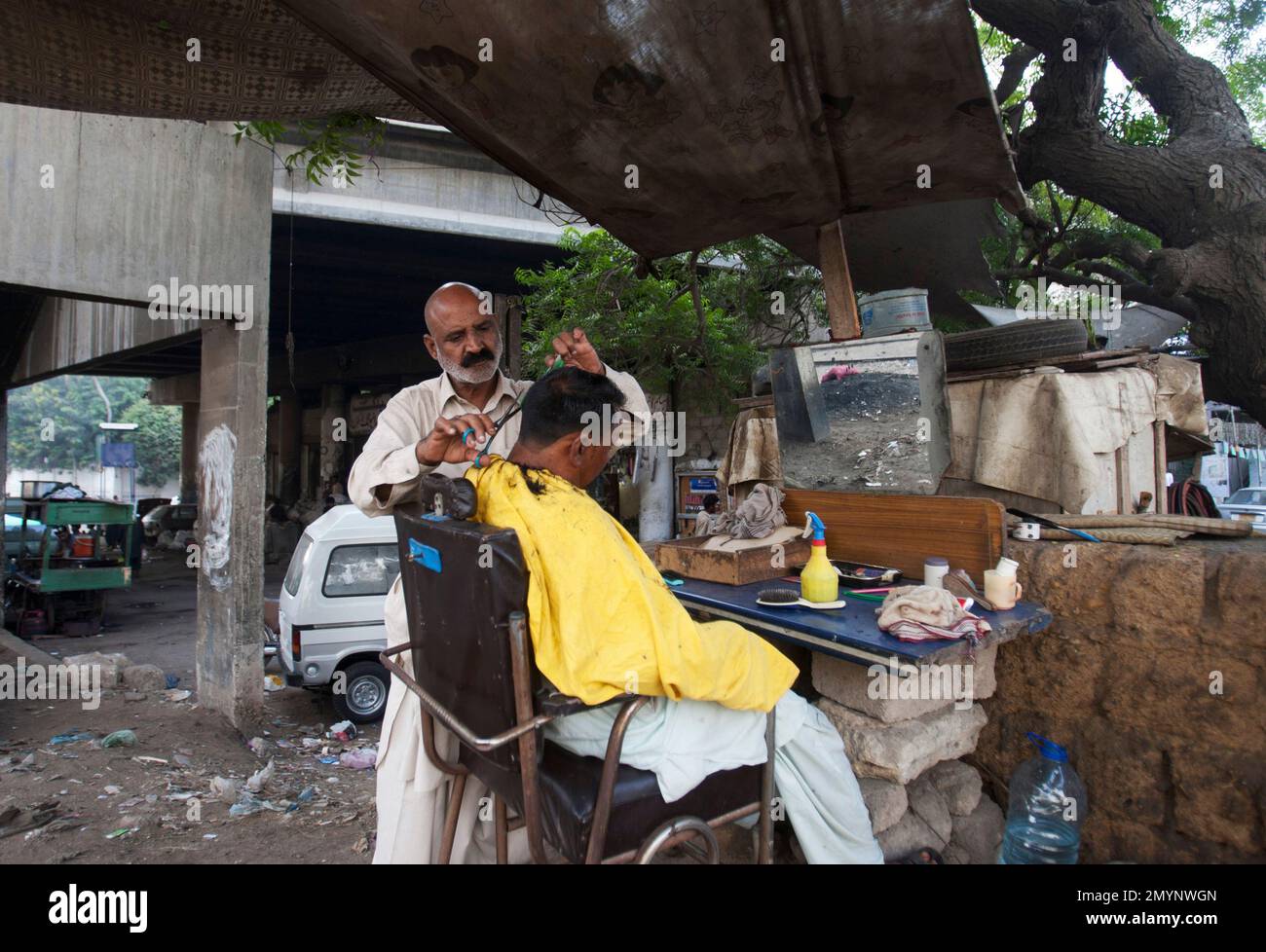 A Pakistani street barber gives a haircut to a customer in Karachi ...