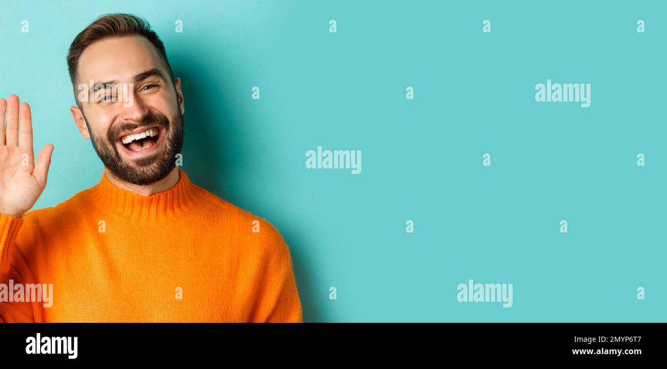 Close-up of friendly young man smiling, waving hand to say hello ...